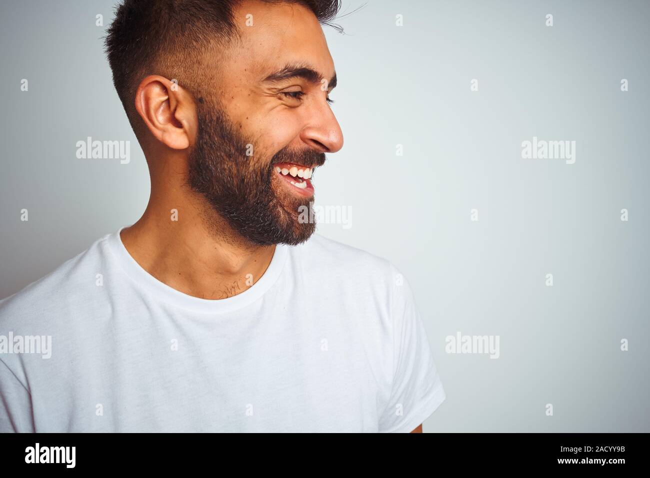 Young indian man wearing t-shirt standing over isolated white ...