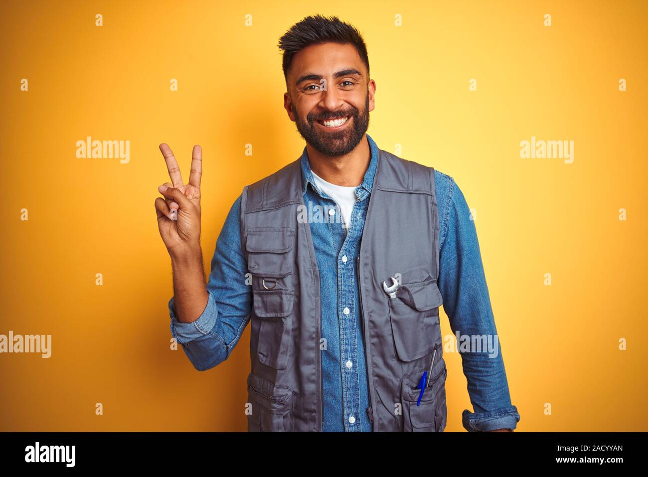Handsome indian technician man wearing uniform over isolated yellow ...