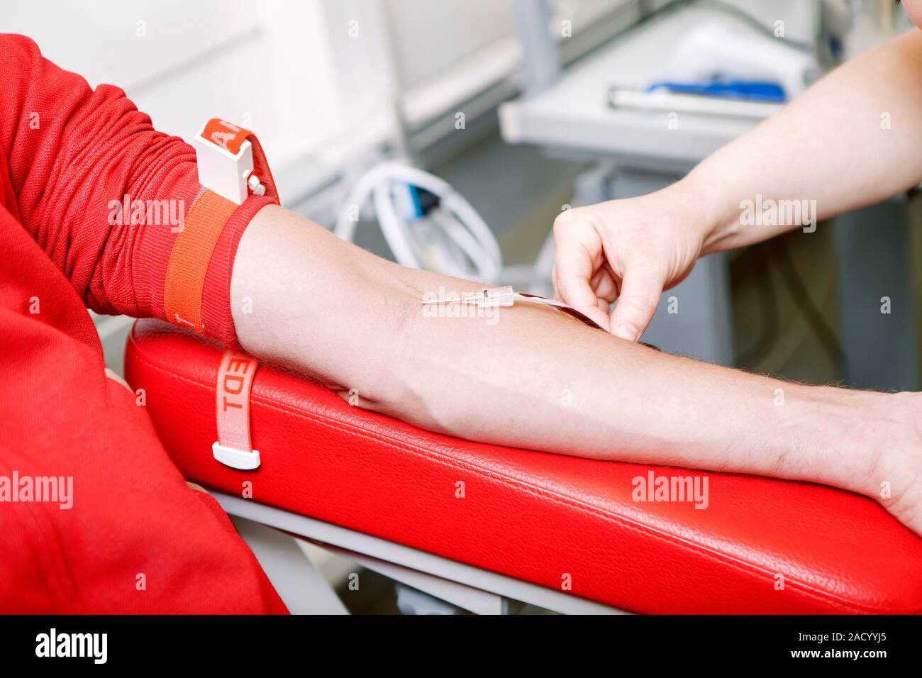 Blood donation clinic. Nurse inserting a cannula into the vein of a man ...