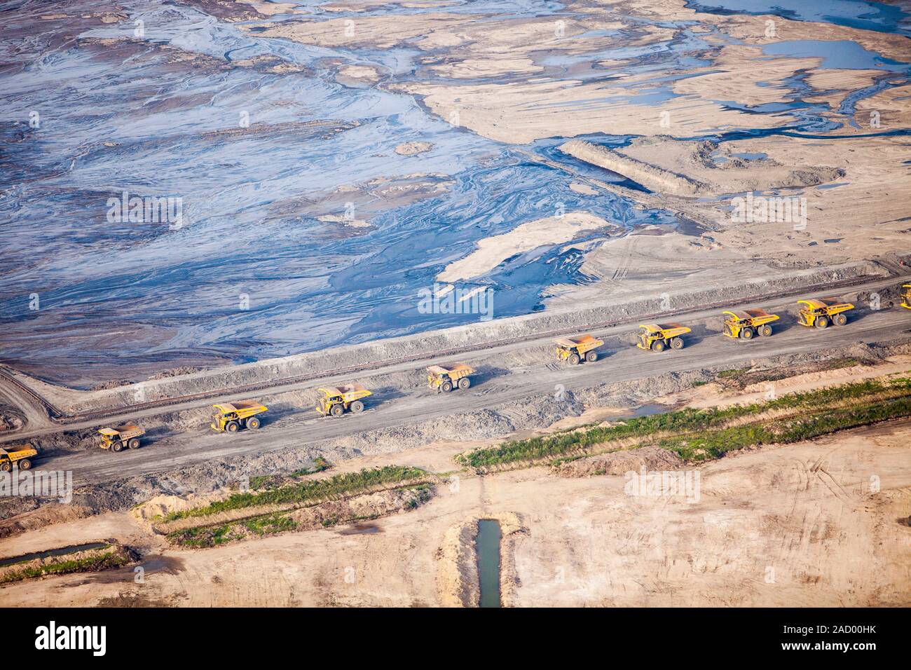 Massive dump trucks queue up to load with tar sand in a mine north of ...