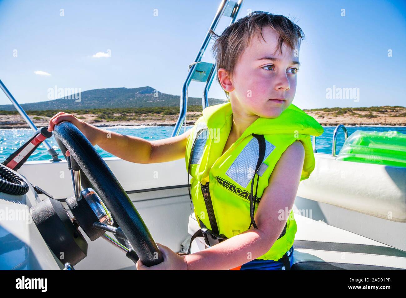 Young boy wearing a florescent life jacket while he drives a speed boat ...