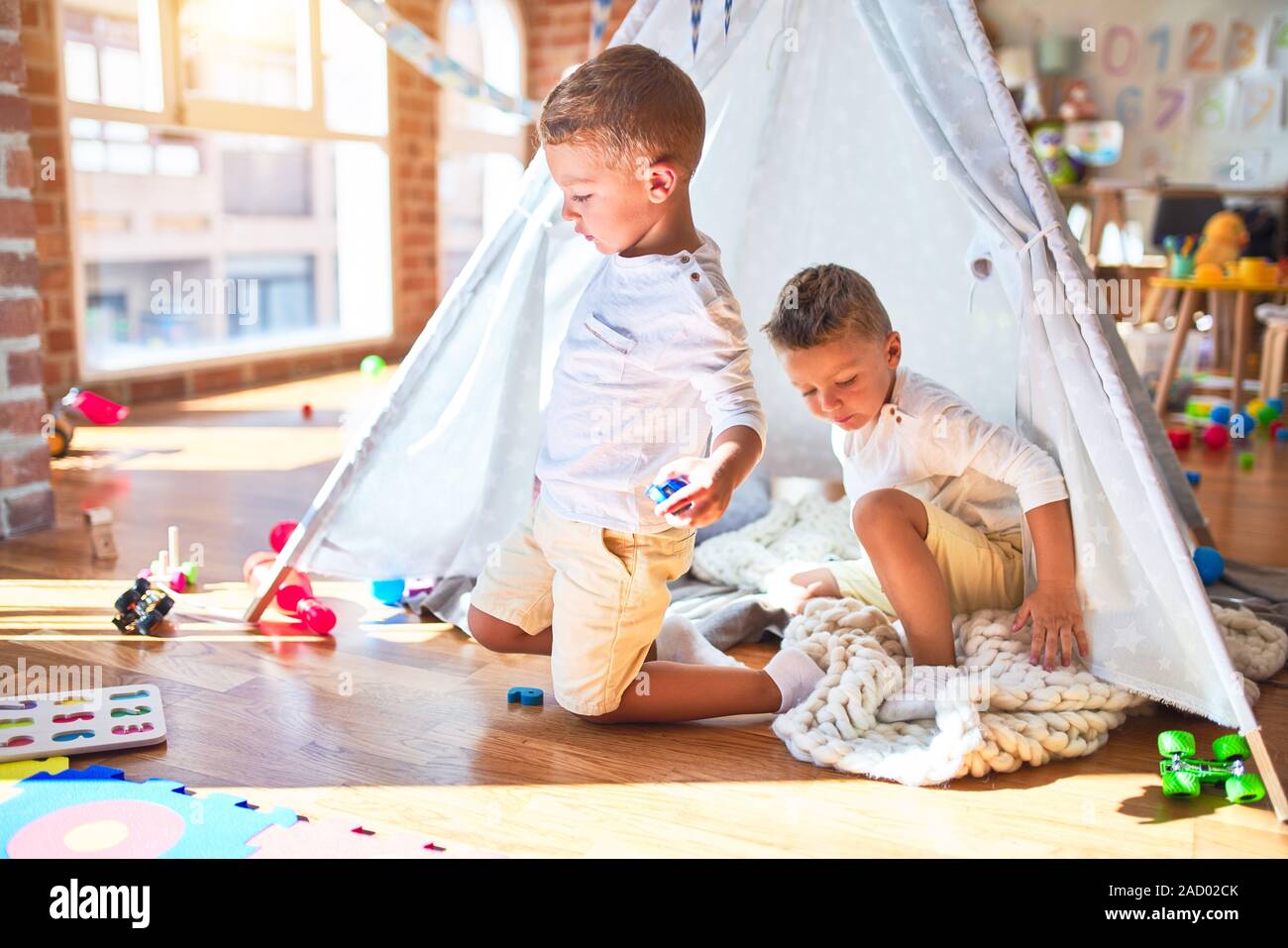 Adorable blonde twins playing inside tipi around lots of toys at ...