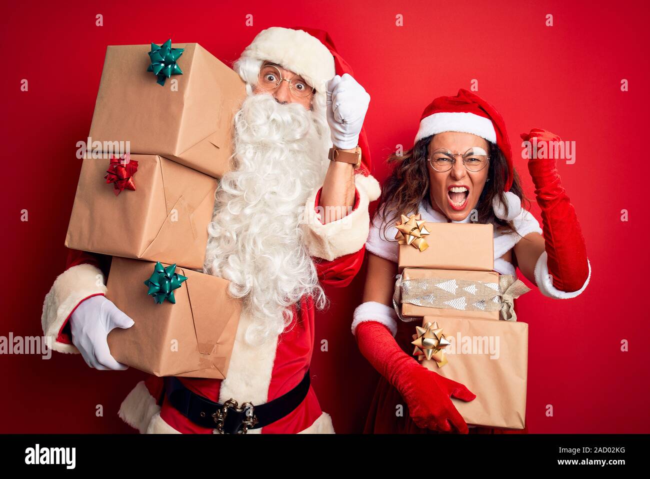 Middle age couple wearing Santa costume holding tower of gifts over ...