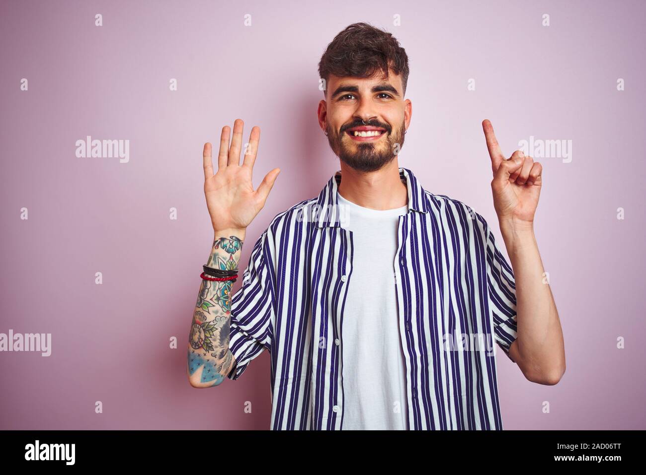 Young man with tattoo wearing striped shirt standing over isolated pink ...