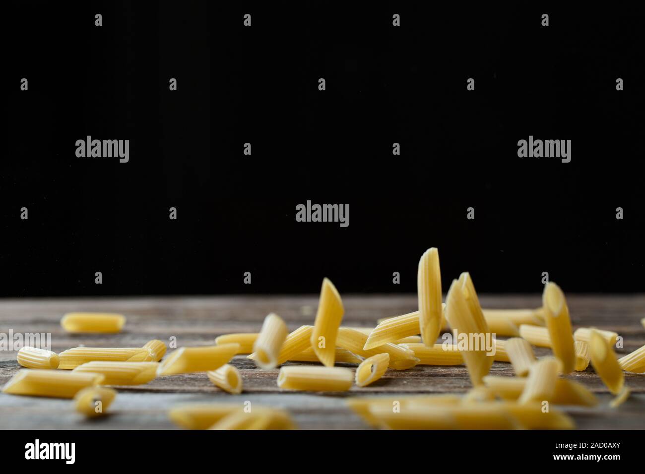 Falling penne pasta. Flying yellow raw macaroni over black background ...