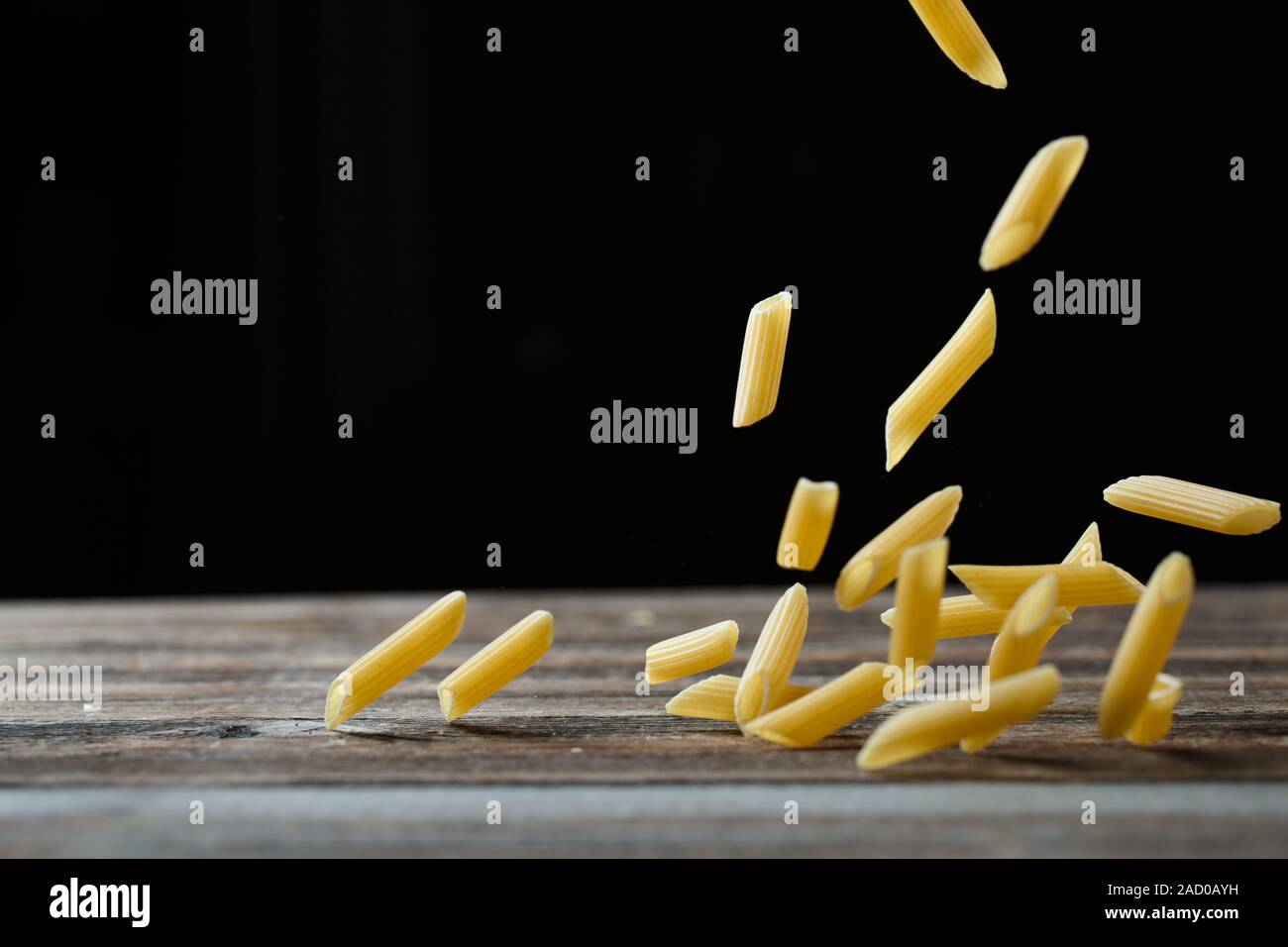 Falling penne pasta. Flying yellow raw macaroni over black background ...