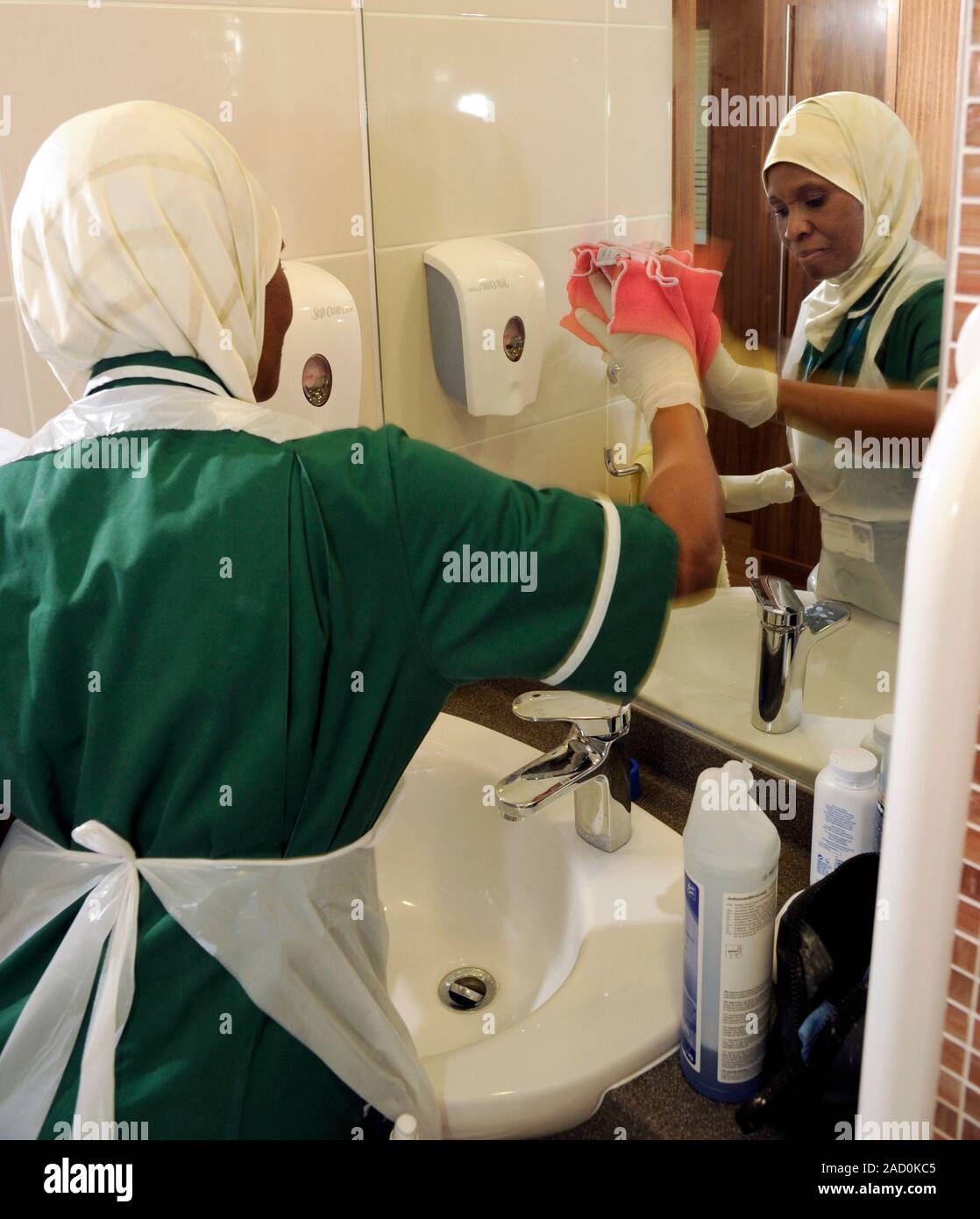 Hospital bathroom cleaning. Hospital cleaner wiping a mirror in a ...