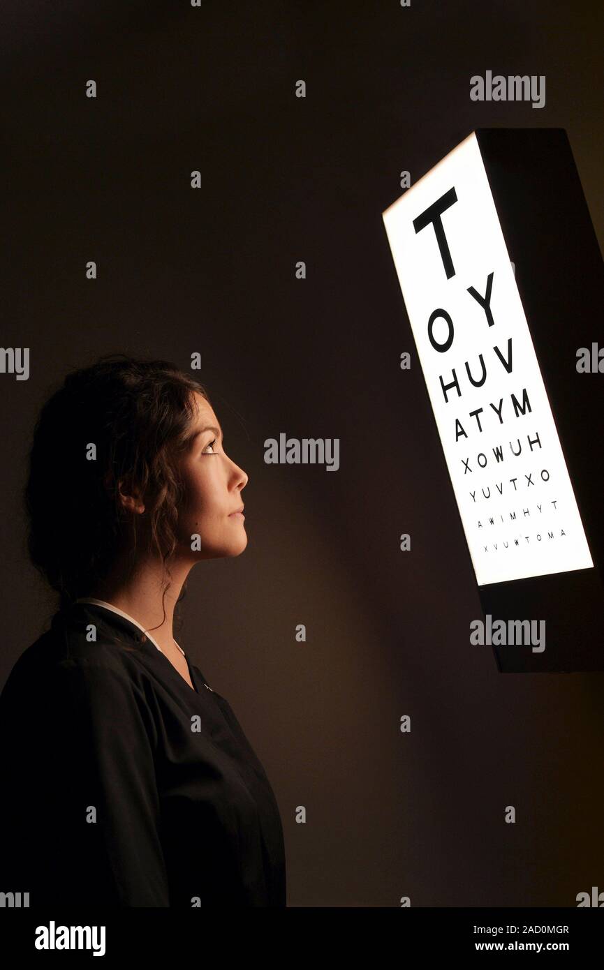 Eye test chart. Woman looking at a backlit chart used in vision tests ...