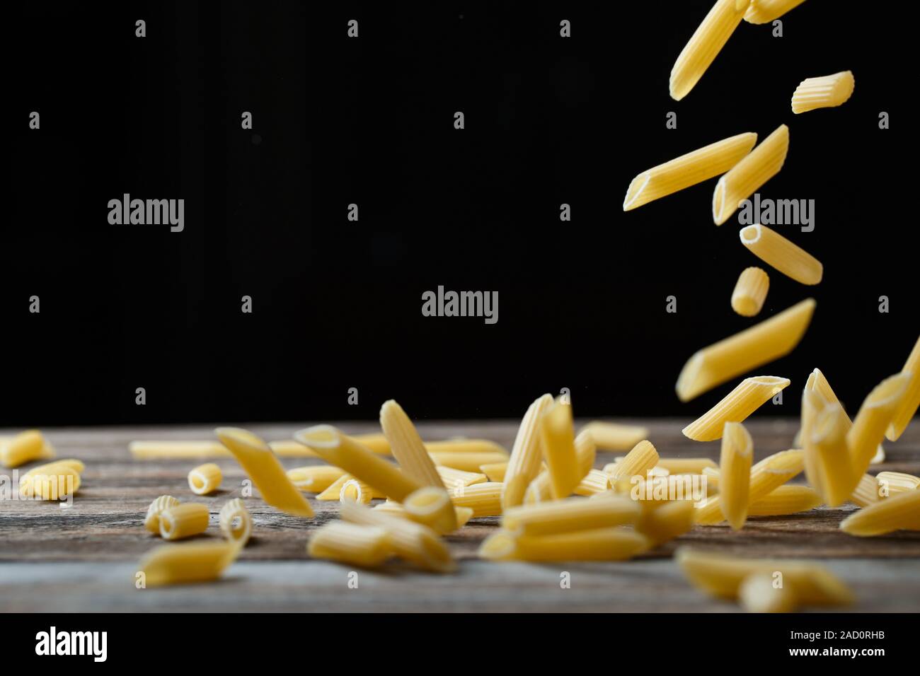 Falling penne pasta. Flying yellow raw macaroni over black background ...