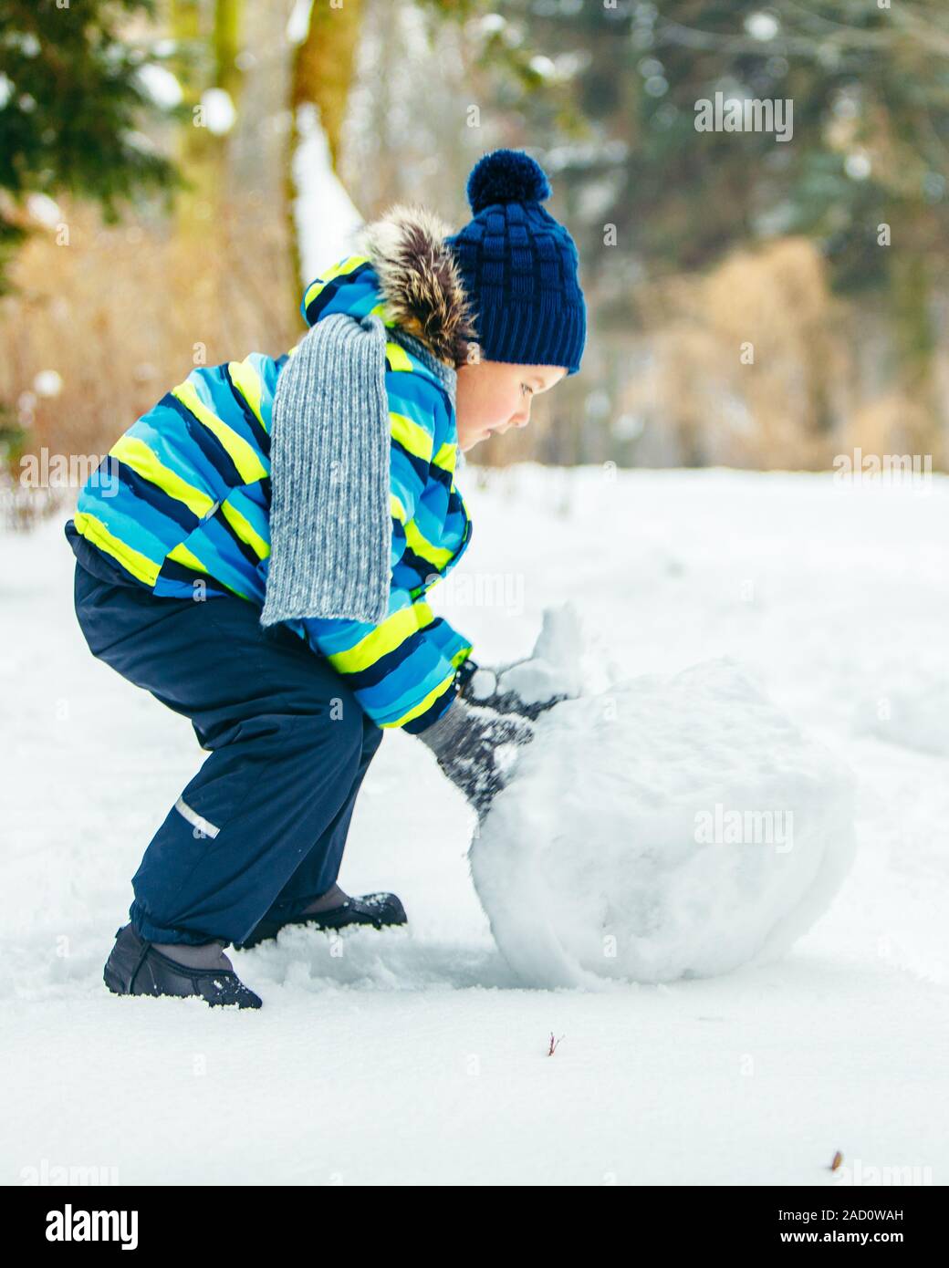 little cute boy making snowman. rolling big snowball Stock Photo - Alamy
