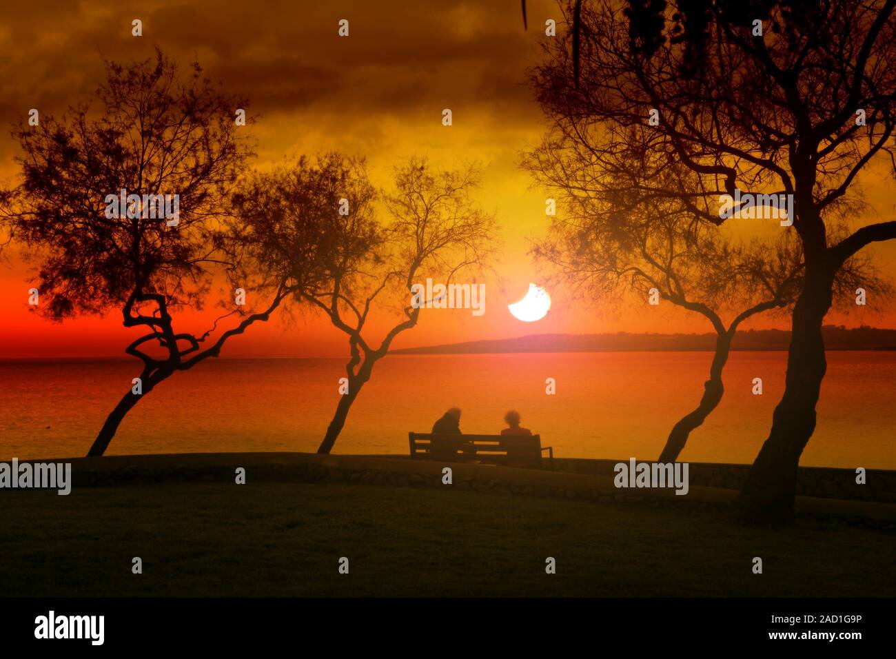 Solar eclipse. People sitting on a bench by the sea watching a partial ...