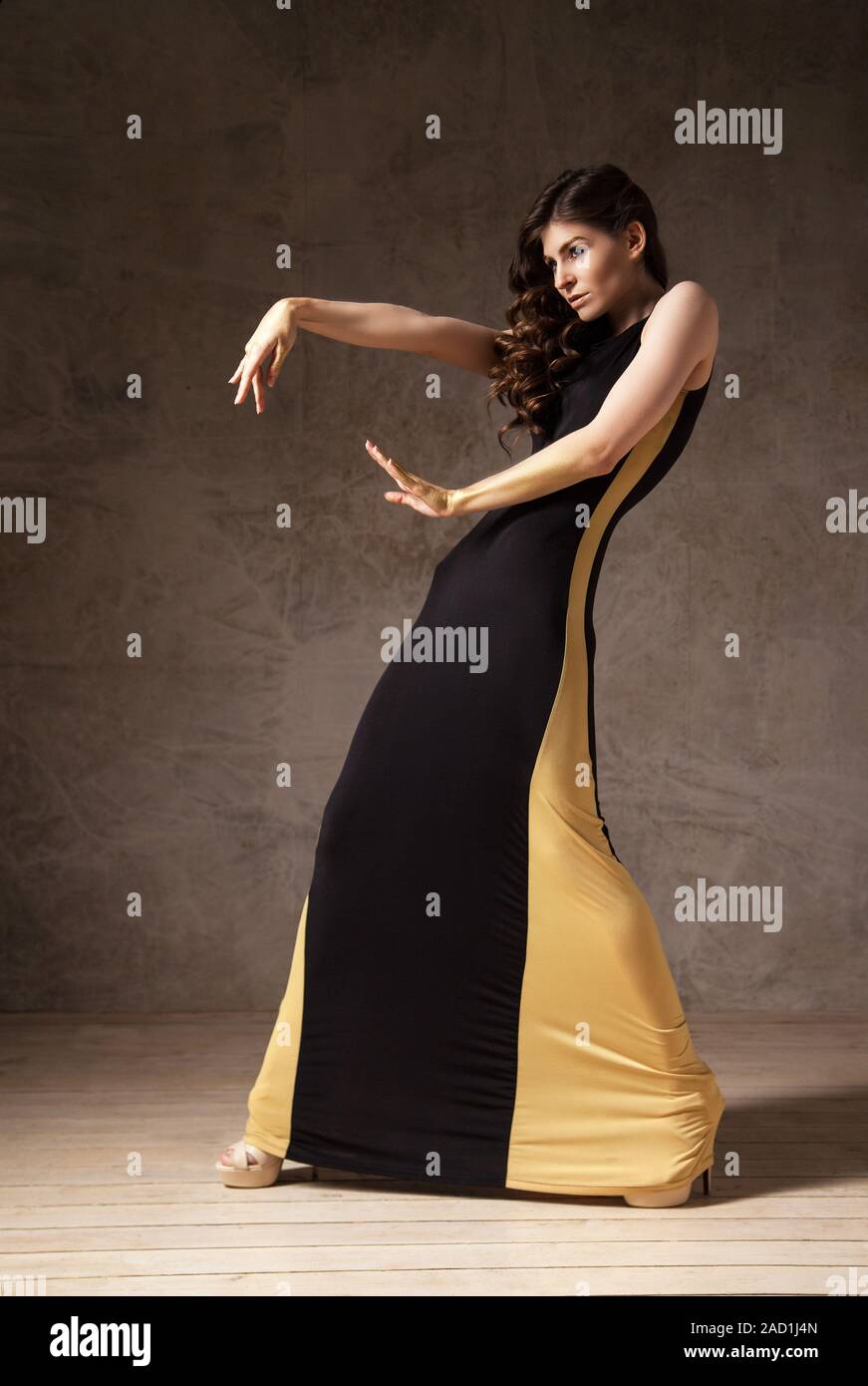 fashion model with wavy hair wearing long dress and gesturing by arms ...