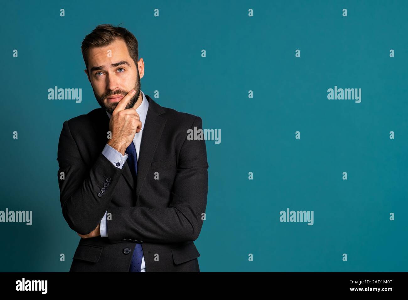 Serious thinking businessman looking around on blue background ...
