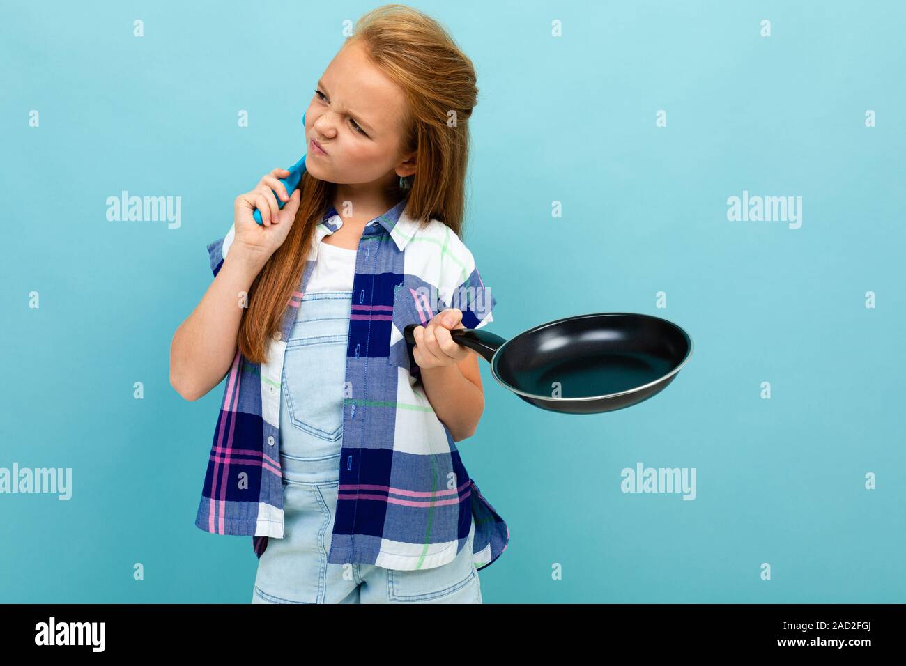 attractive european girl with a frying pan in hands on a light blue ...