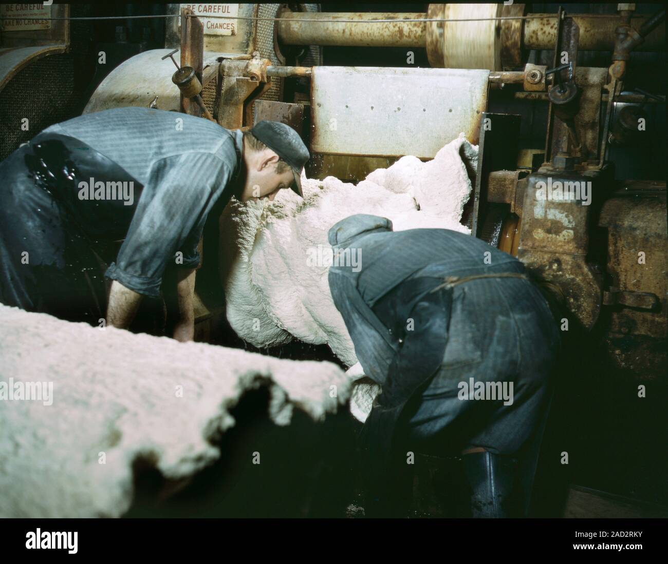 Synthetic rubber production. Workers handling a sheet of synthetic ...