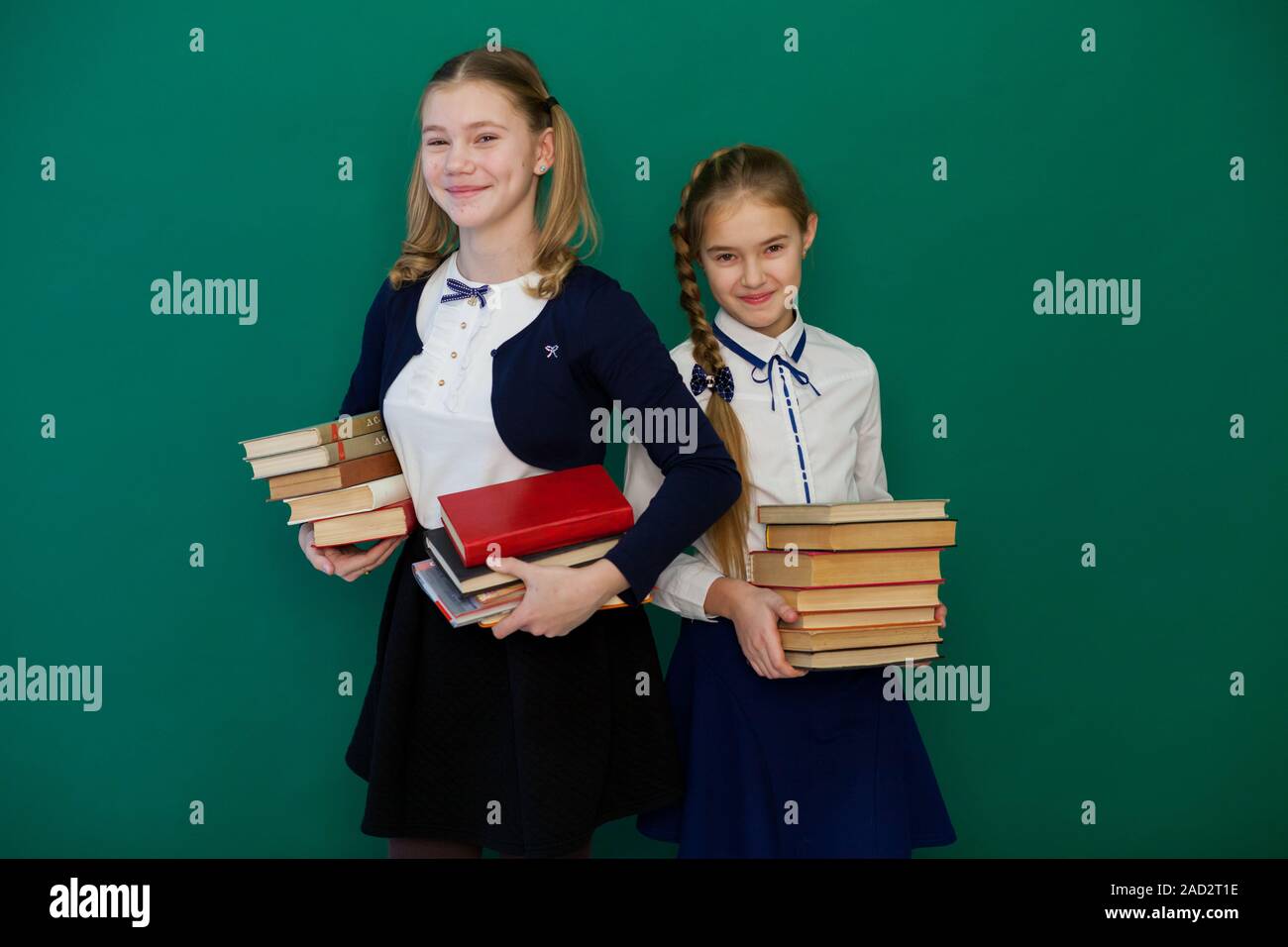 two girls of schoolgirls with books to study stands at the green board ...