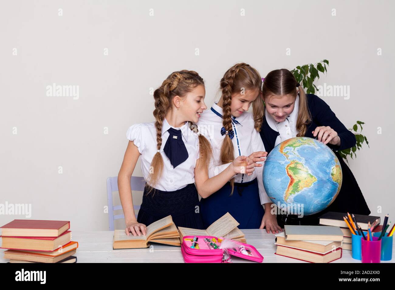 three girls of the school with books for studying sit at the desk in ...
