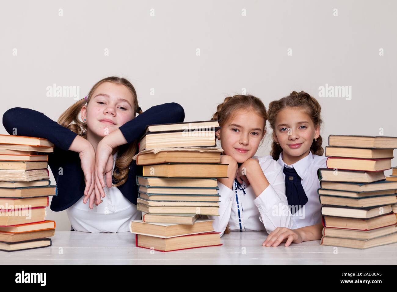 three girls of school girls with books for study sit at the desk in the ...