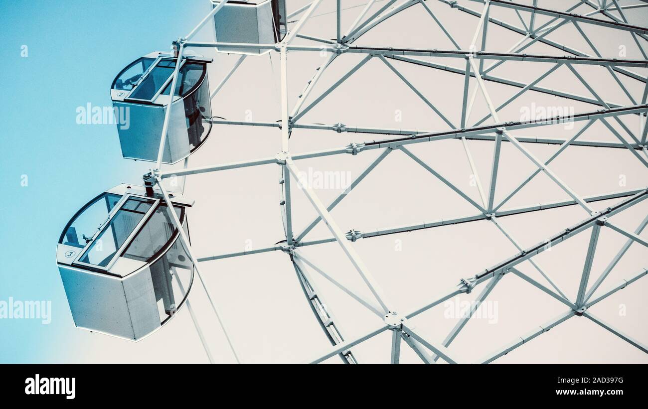 Ferris wheel with booths for visitors spinning against the blue sky ...