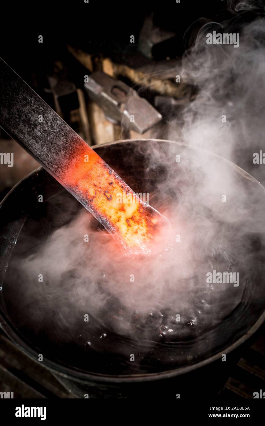 Blacksmith at work in a forge. Red-hot metal being quenched in a ...
