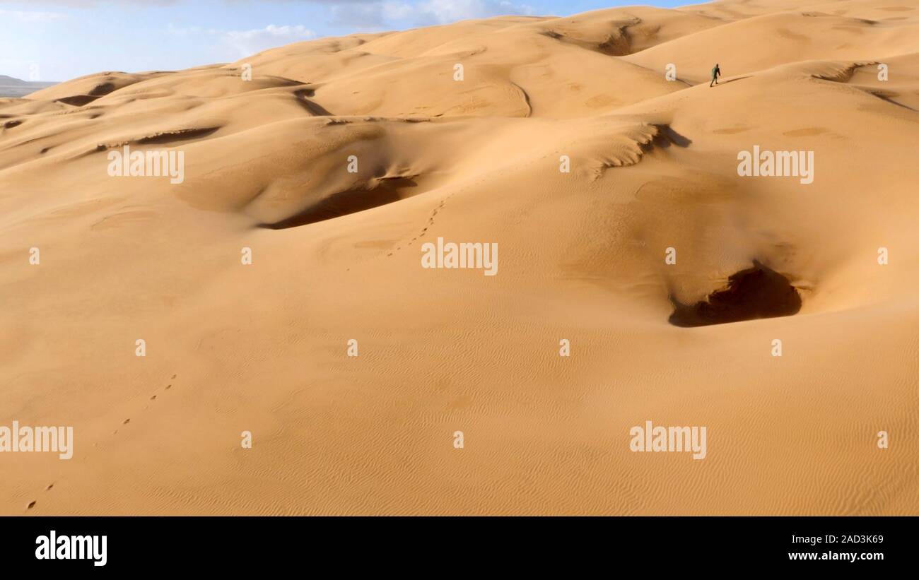 Barchan dunes. Man climbing a large barchan dune ('mega barchan') in ...
