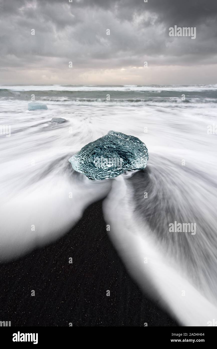 Round ice block in blue tones on a beach with strong surf, the water ...