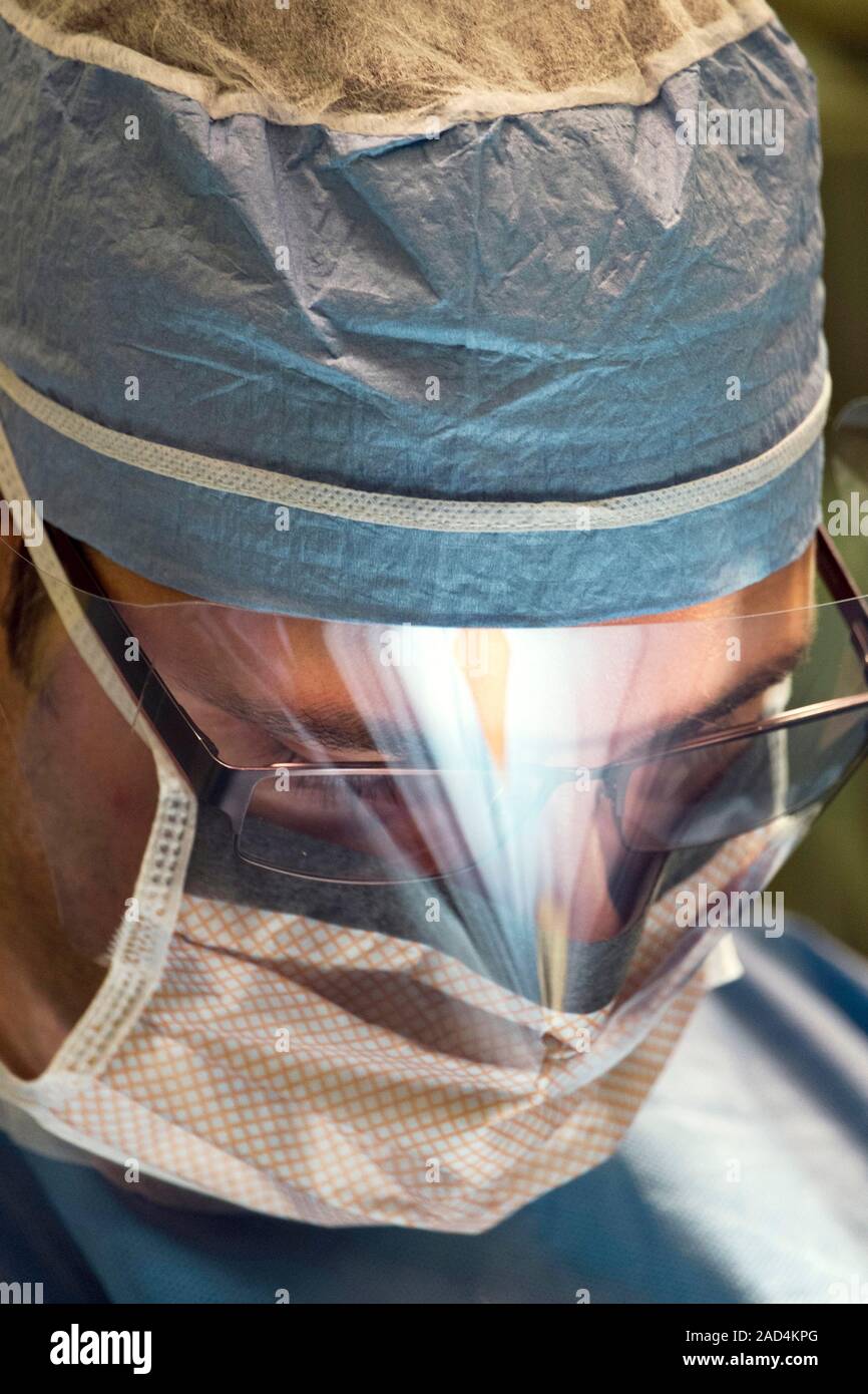 Surgeon wearing a visor, a face mask and surgical drapes during surgery ...