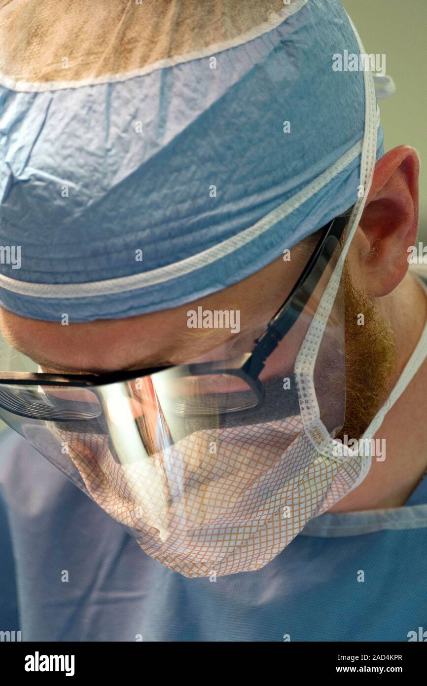 Surgeon wearing a visor, a face mask and surgical drapes during surgery ...
