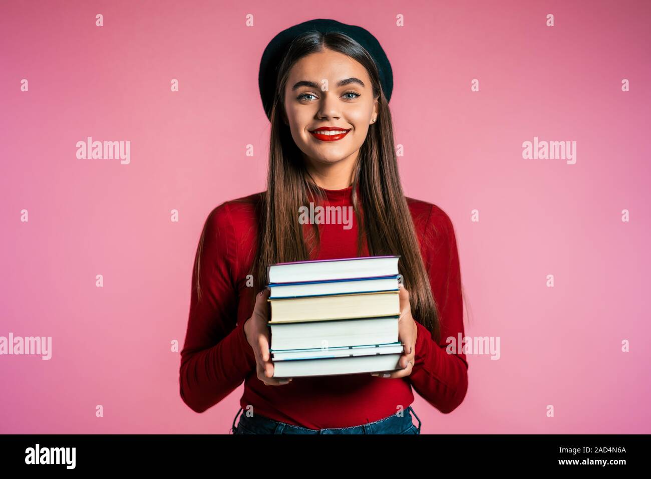 Pretty student on pink background in studio holds stack of university ...