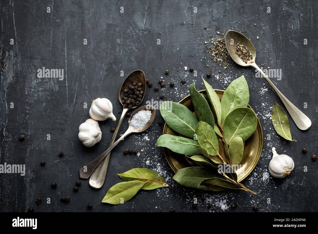 Dark culinary background with bay leaves, salt, pepper and garlic, view ...