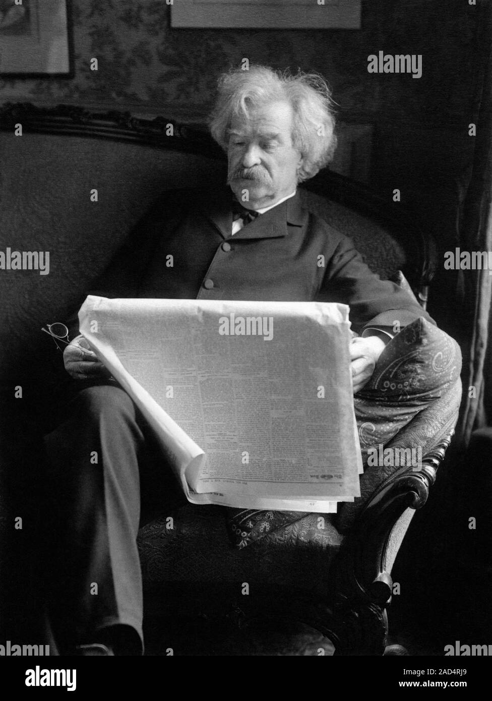 Mark Twain (1835-1910), US author and novelist, seated reading a ...