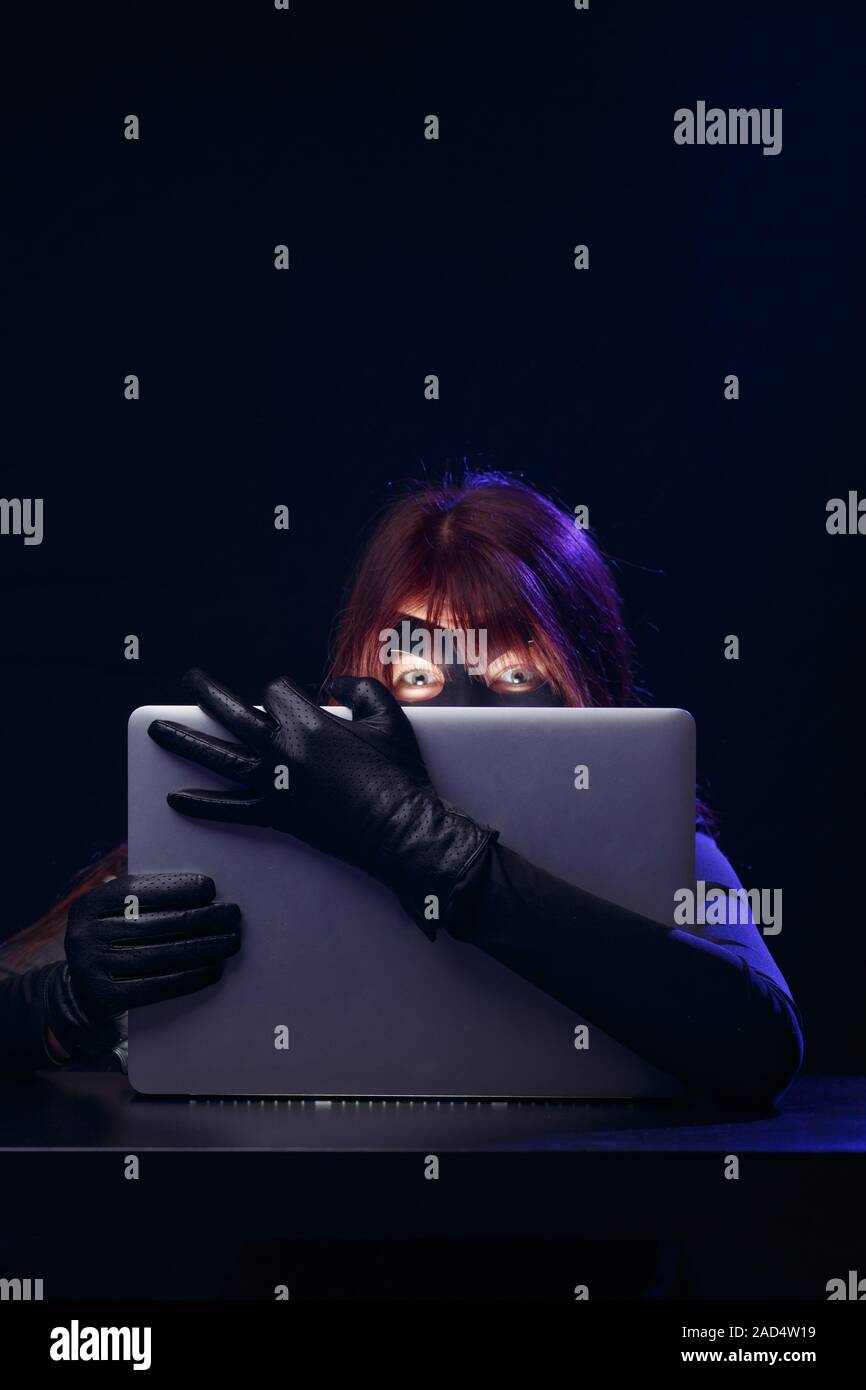 Hacker in mask holds laptop Stock Photo - Alamy