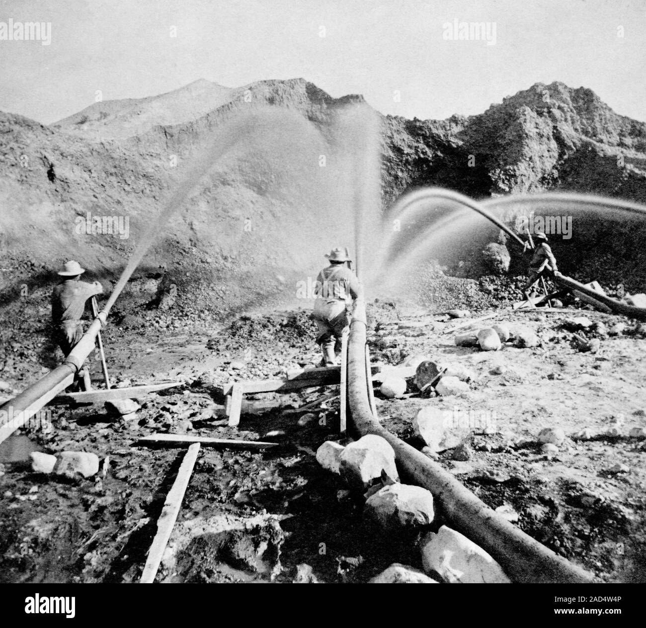 Hydraulic mining. Miners using high-pressure water hoses to dislodge ...
