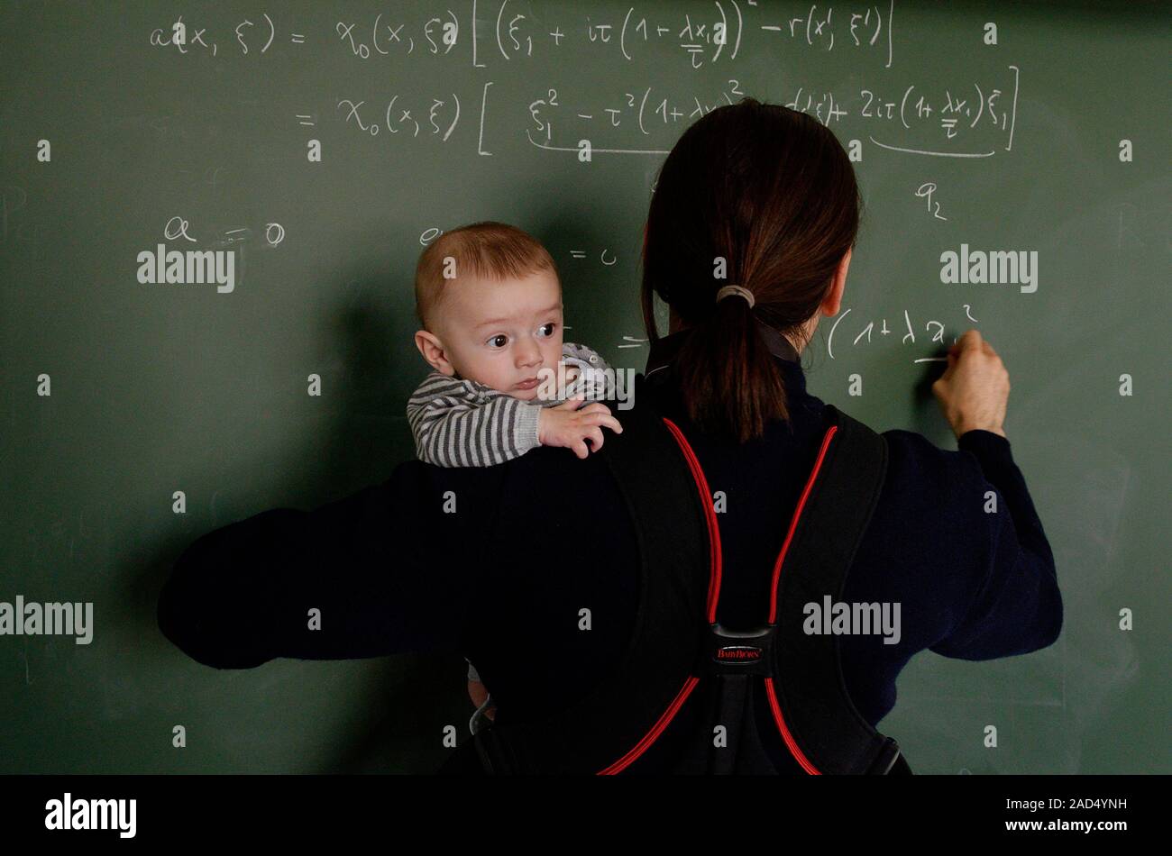 Mathematics education. A woman holding her baby writes an equation on a ...