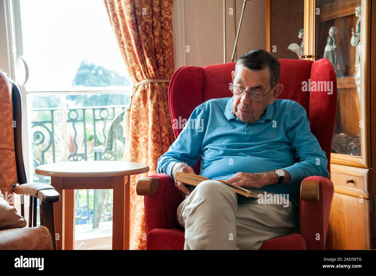 Care home resident. 88-year-old man sitting and reading a book in a ...