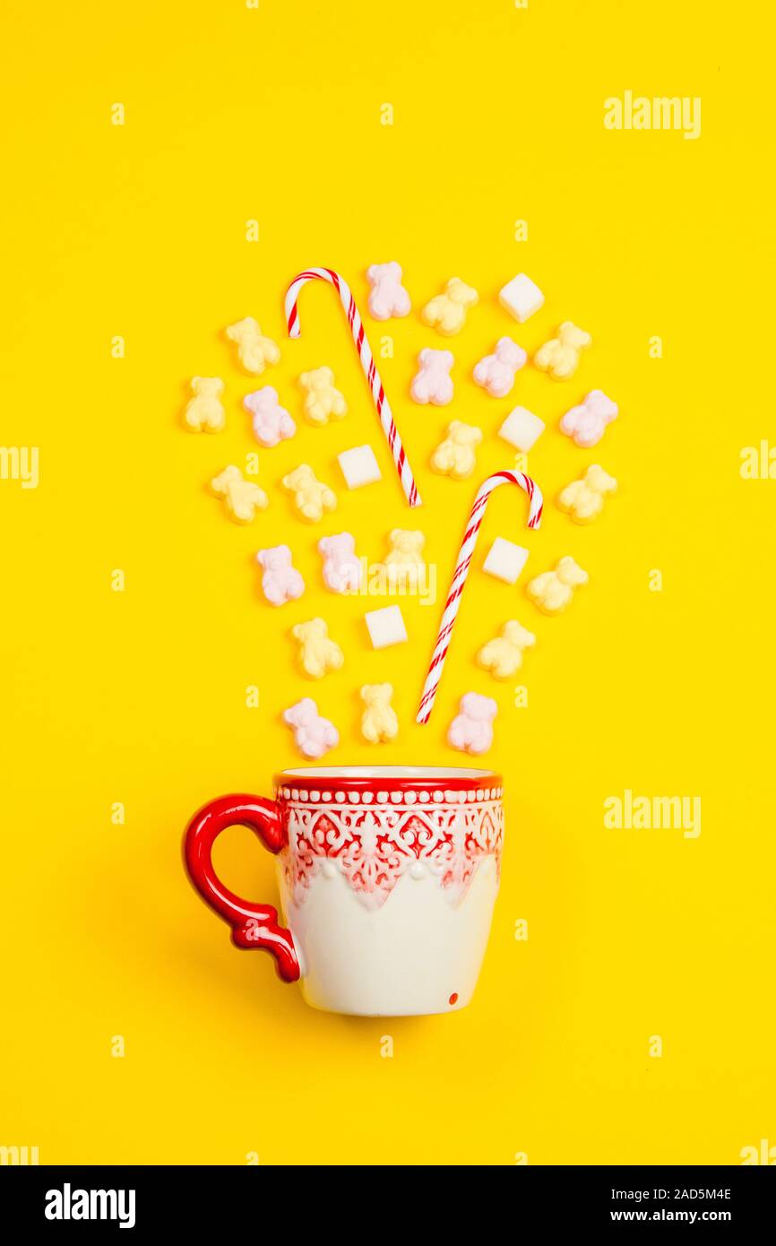 Marshmallows, sugar cubes and candy sticks in a holiday mug on a yellow ...