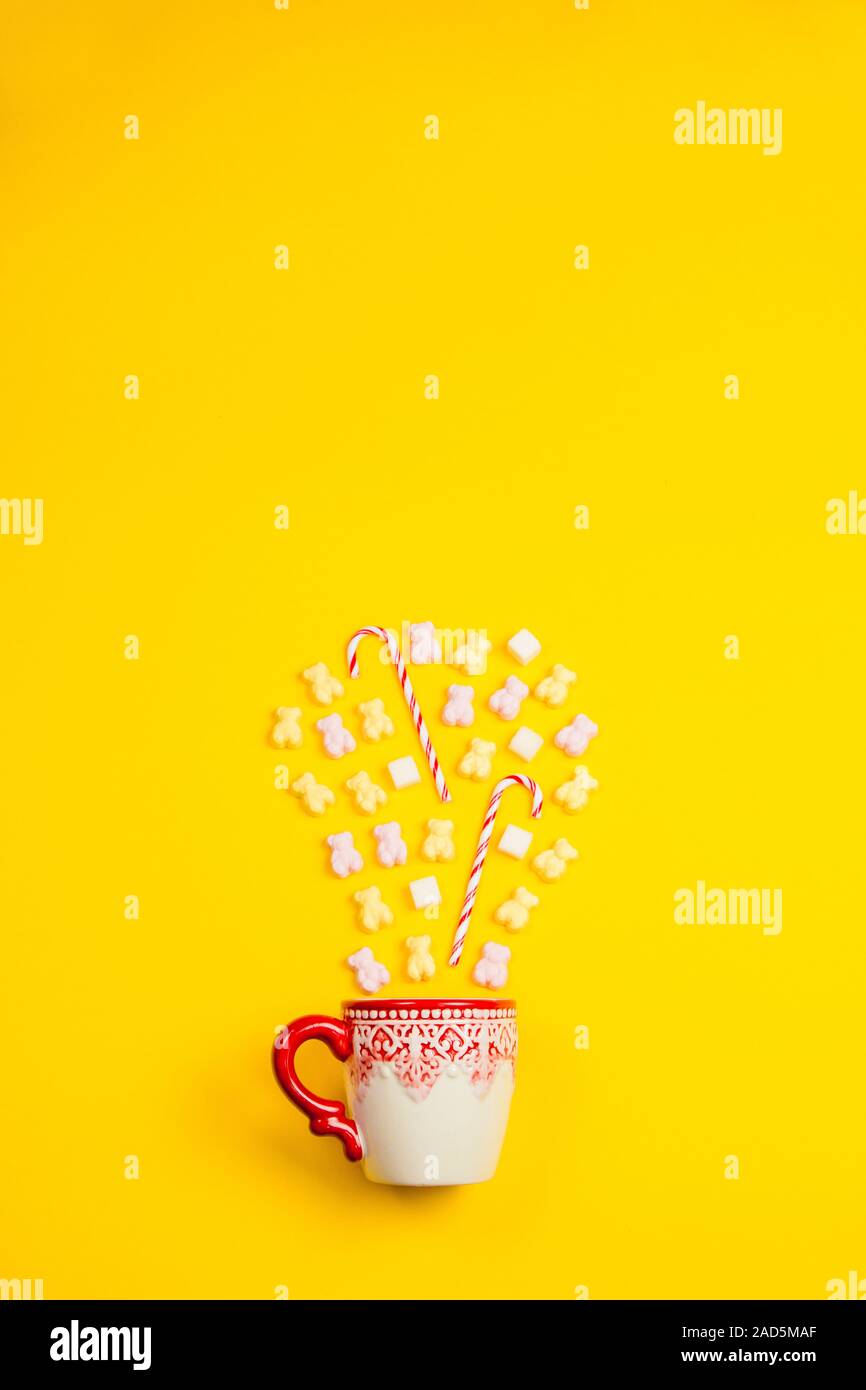 Marshmallows, sugar cubes and candy sticks in a holiday mug on a yellow ...