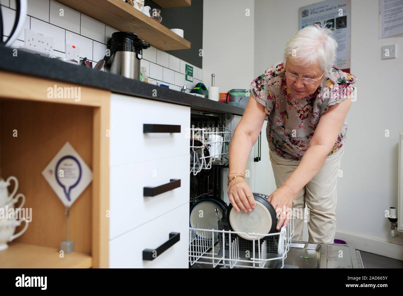 Dementia-friendly kitchen. Woman with dementia loading the dishwasher ...