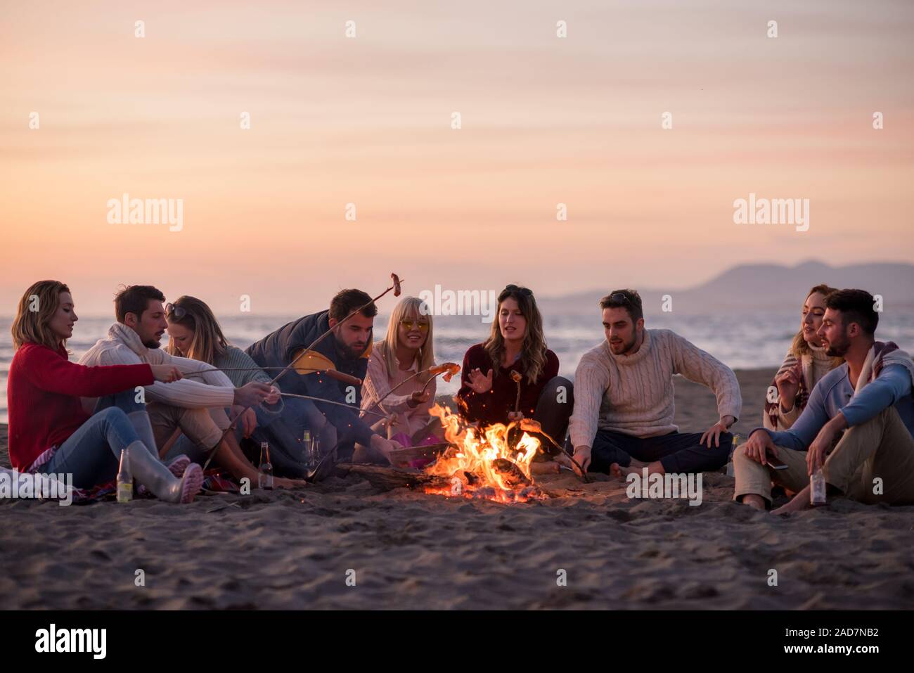 Group Of Young Friends Sitting By The Fire at beach Stock Photo - Alamy