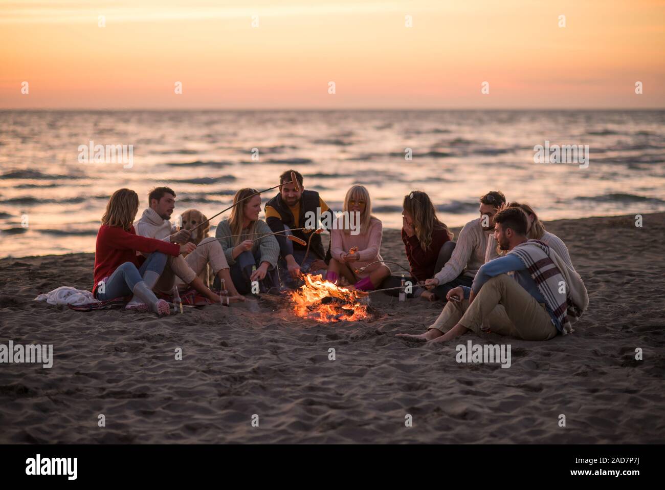 Group Of Young Friends Sitting By The Fire at beach Stock Photo - Alamy
