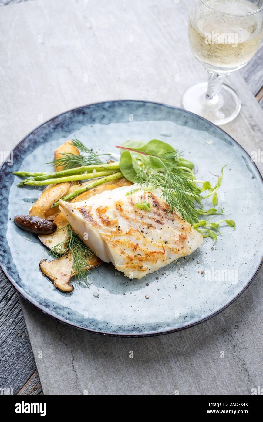Fried cod fish filet with green asparagus and mushrooms as close up on ...