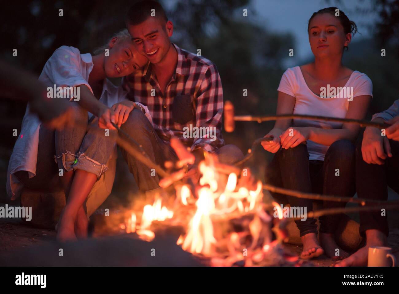 young friends relaxing around campfire Stock Photo - Alamy