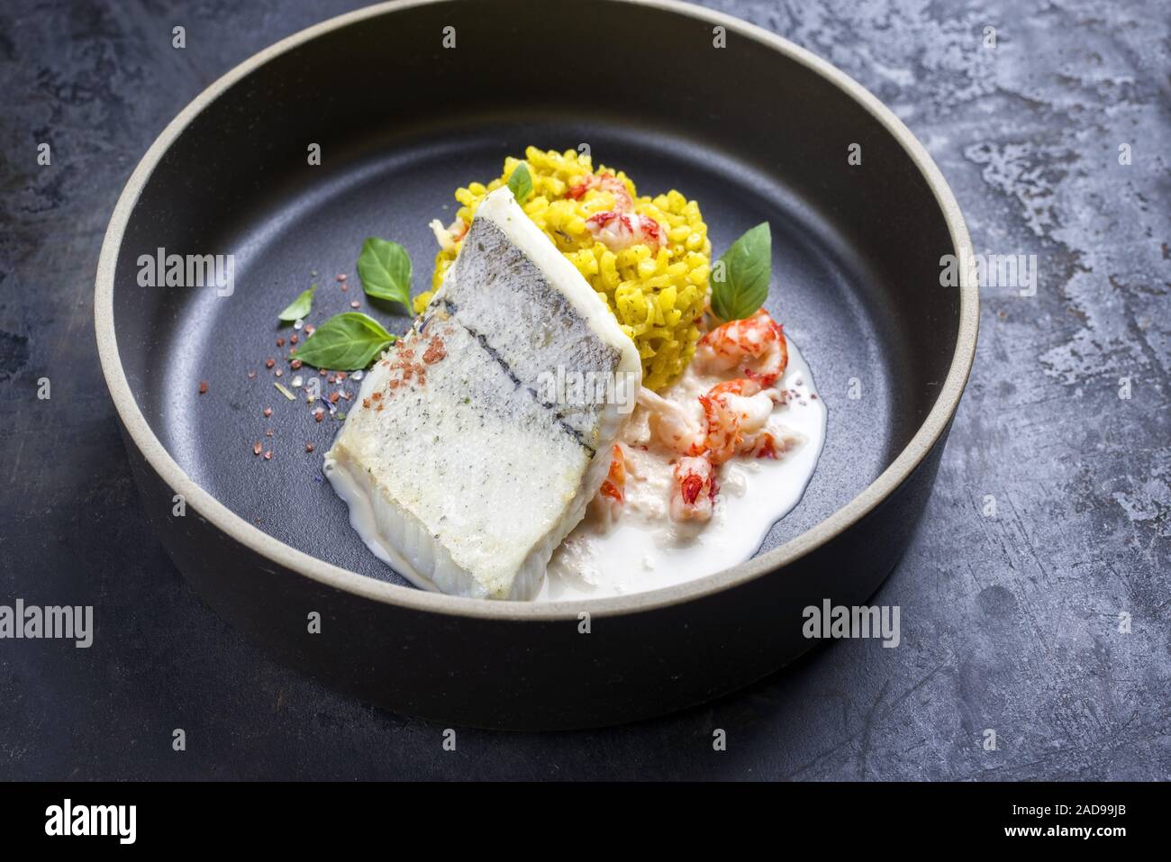 Fried haddock filet with saffron rice and shell prawns in crab sauce as ...