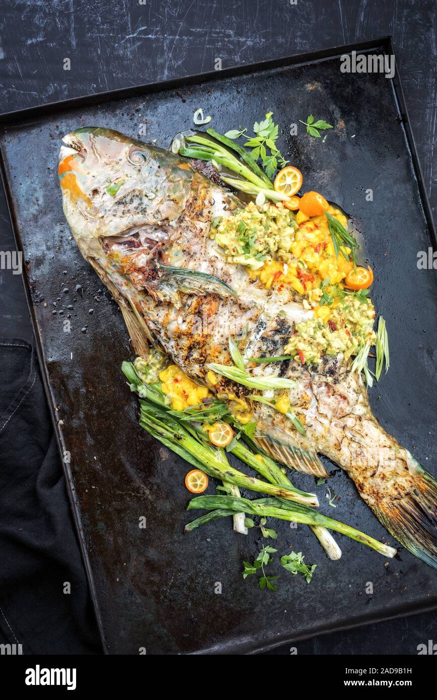 Traditional BBQ parrotfish with mango salsa as top view on a black ...