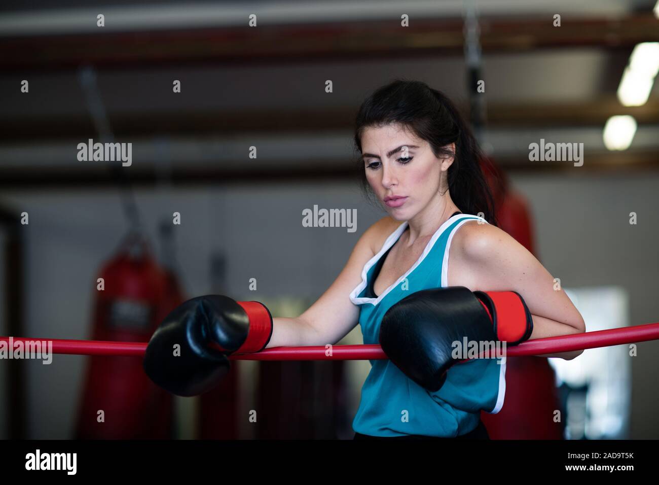 A young woman girl is hanging on the ropes of a boxing ring, resting ...