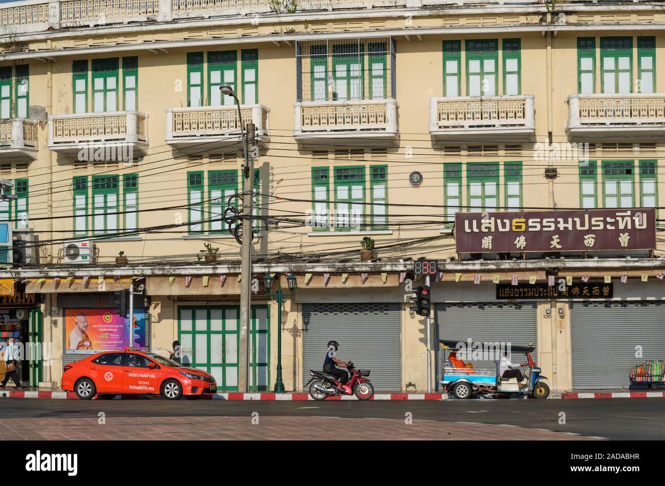 An orange taxi, a tuk-tuk and a motorcyclist pass an imposing heritage ...