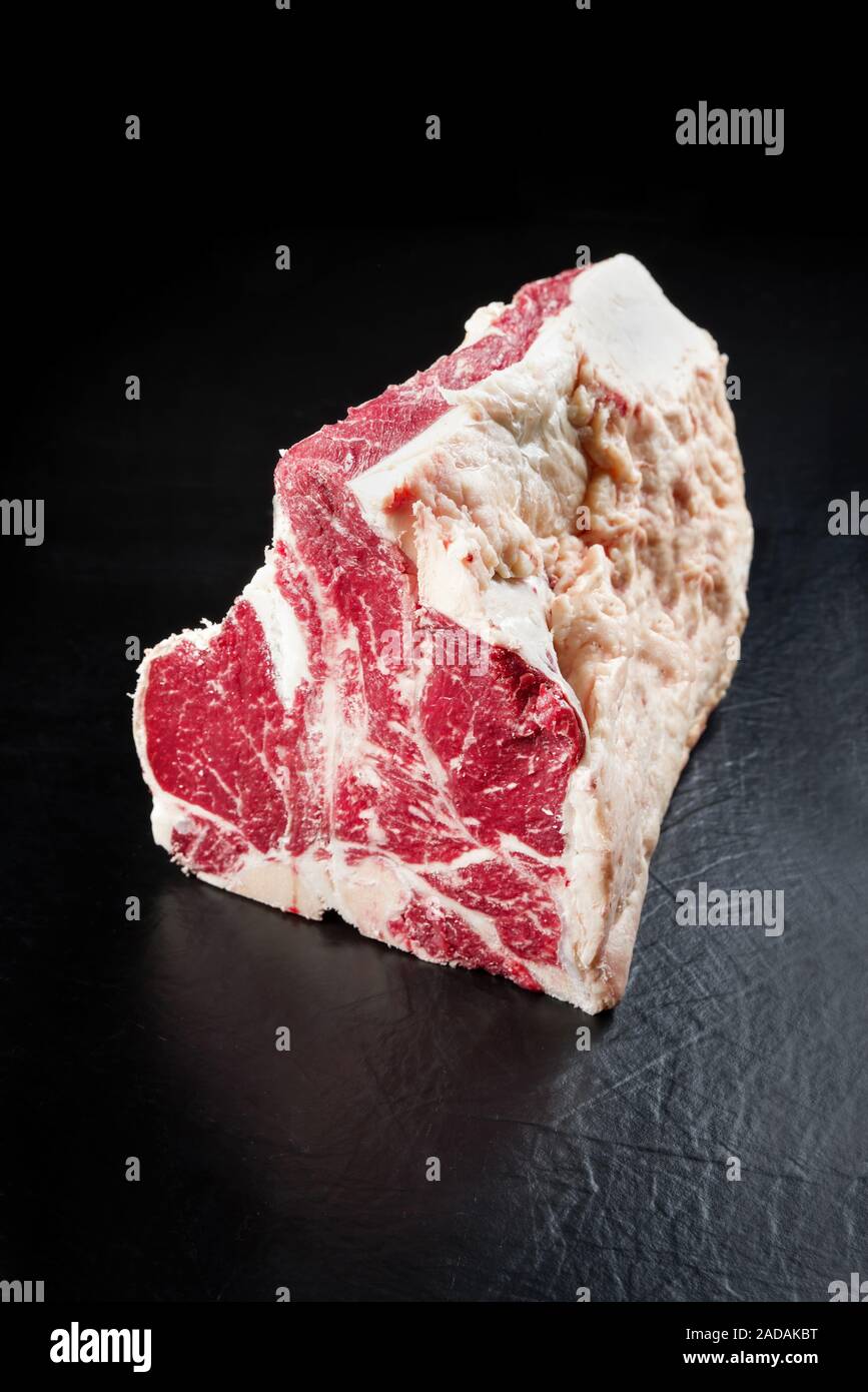 Raw dry aged wagyu porterhouse beef block as closeup on black ...