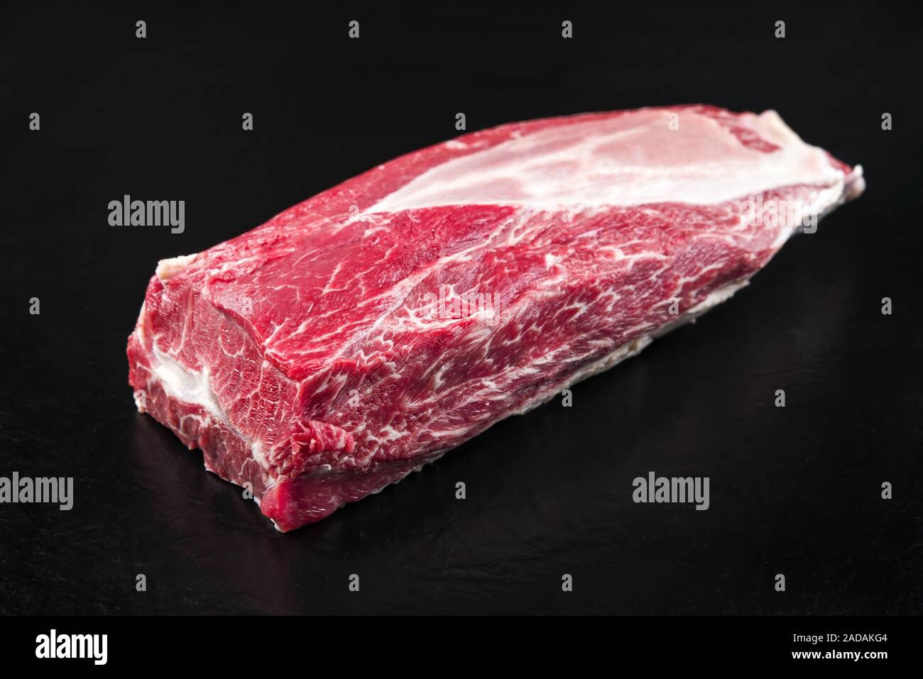 Raw dry aged wagyu beef top blade roast as closeup on black background ...