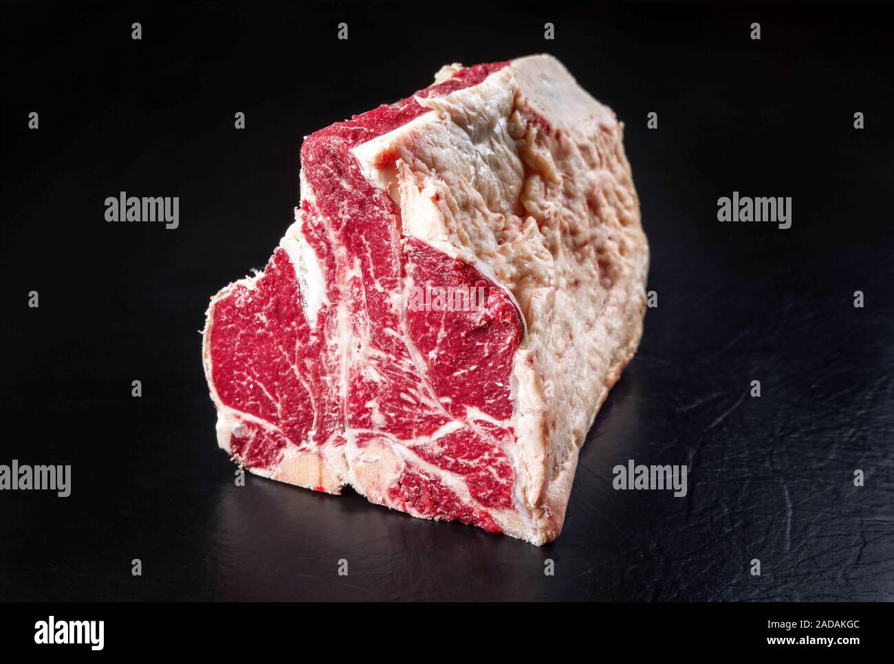 Raw dry aged wagyu porterhouse beef block as closeup on black ...