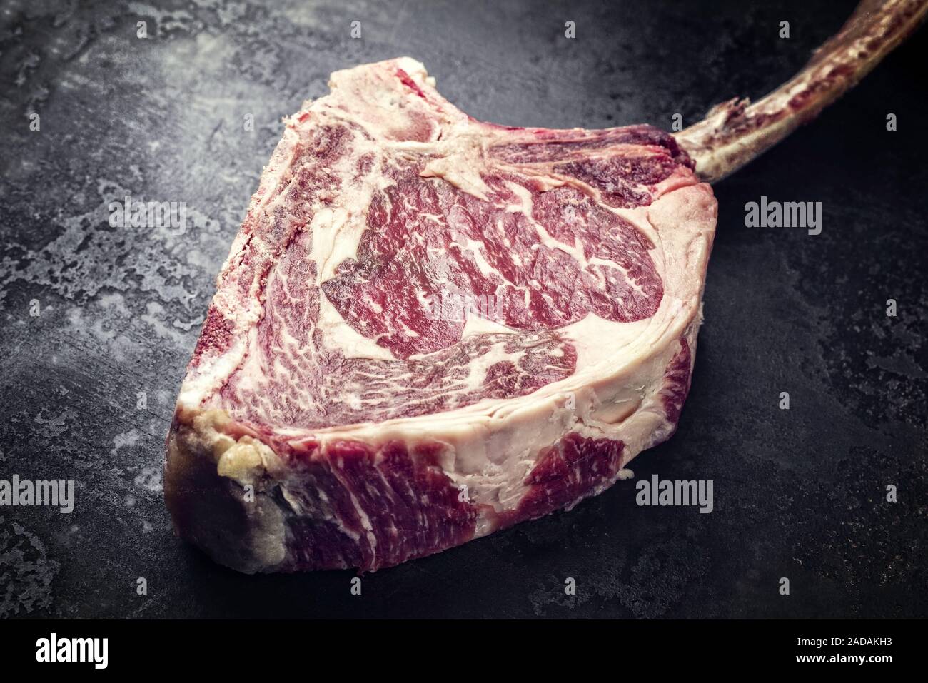 Raw dry aged wagyu tomahawk steak as closeup on an old rustic board ...